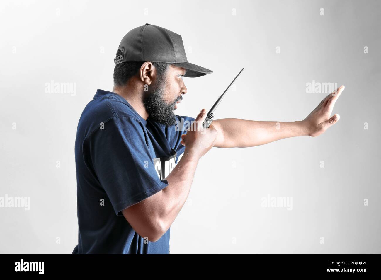 Male security guard showing stop gesture while using portable radio, on ...