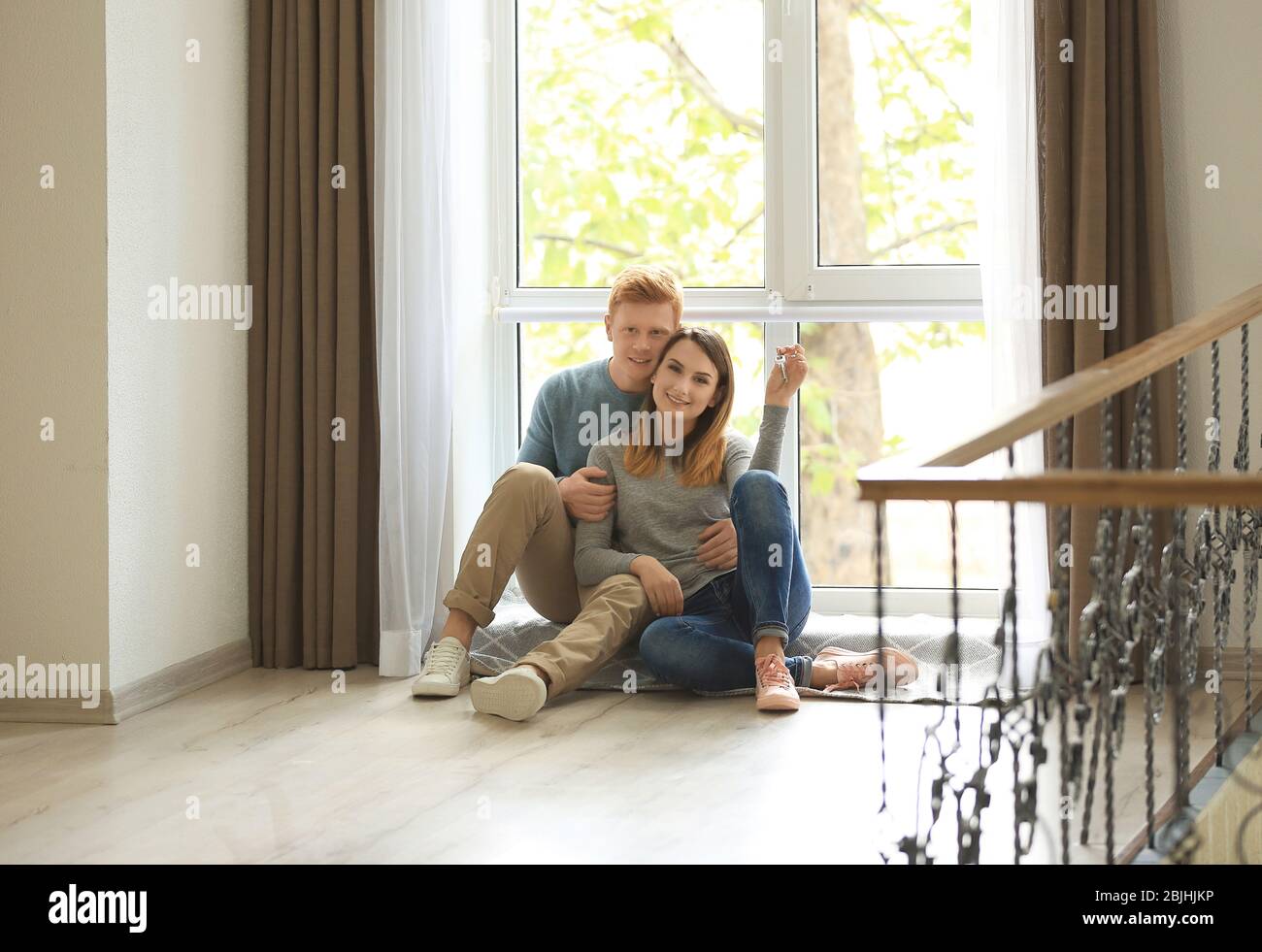 Lovely couple sitting near window with keys from new flat Stock Photo ...