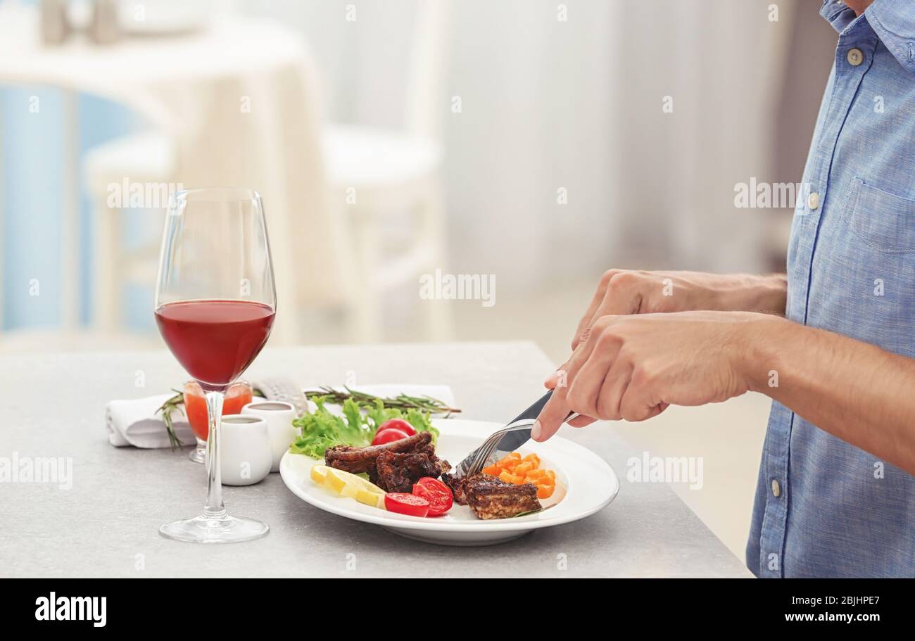 Young man eating delicious roasted ribs in restaurant Stock Photo - Alamy