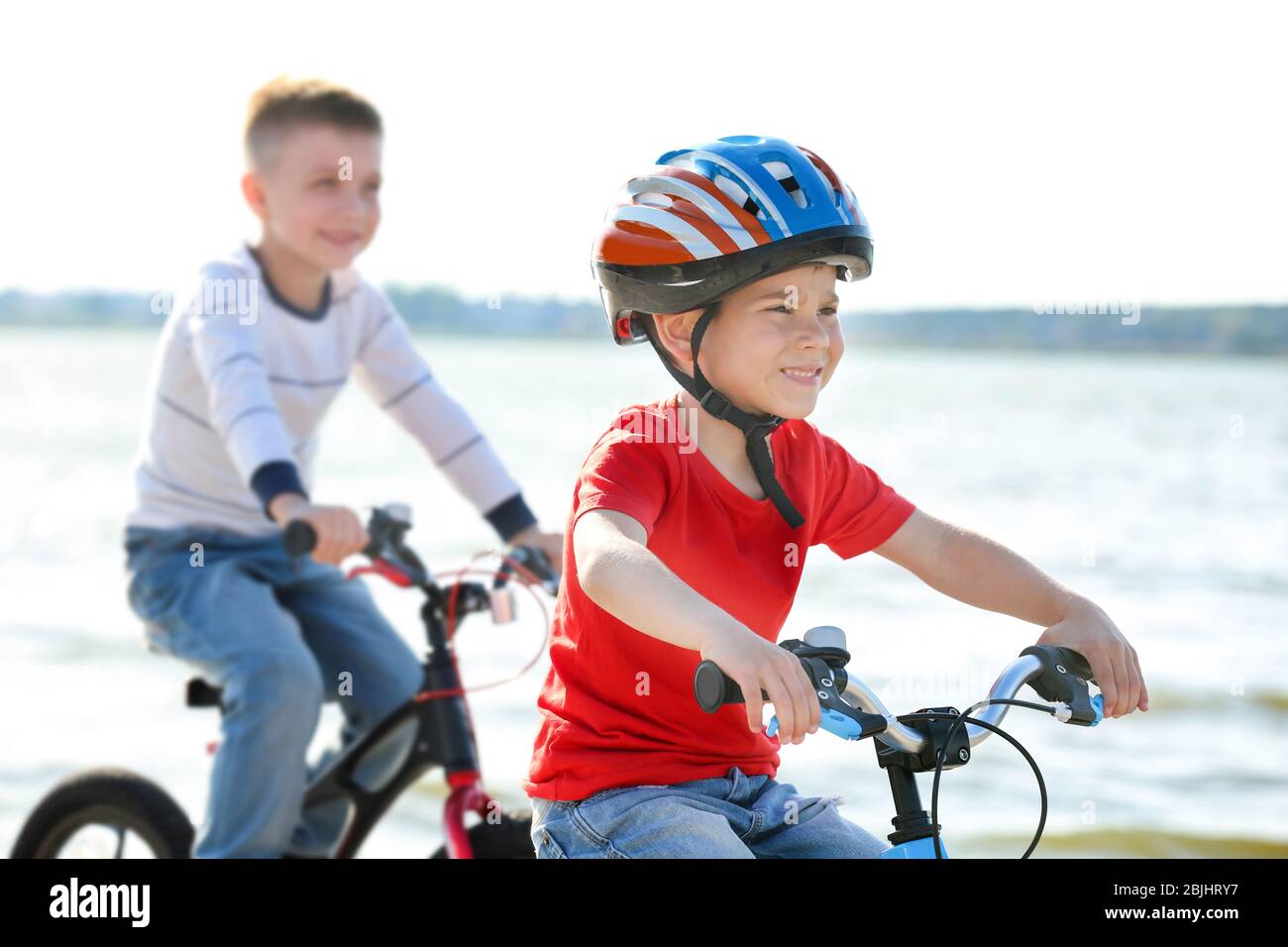 Cute little boys riding bicycles near river on sunny day Stock Photo ...