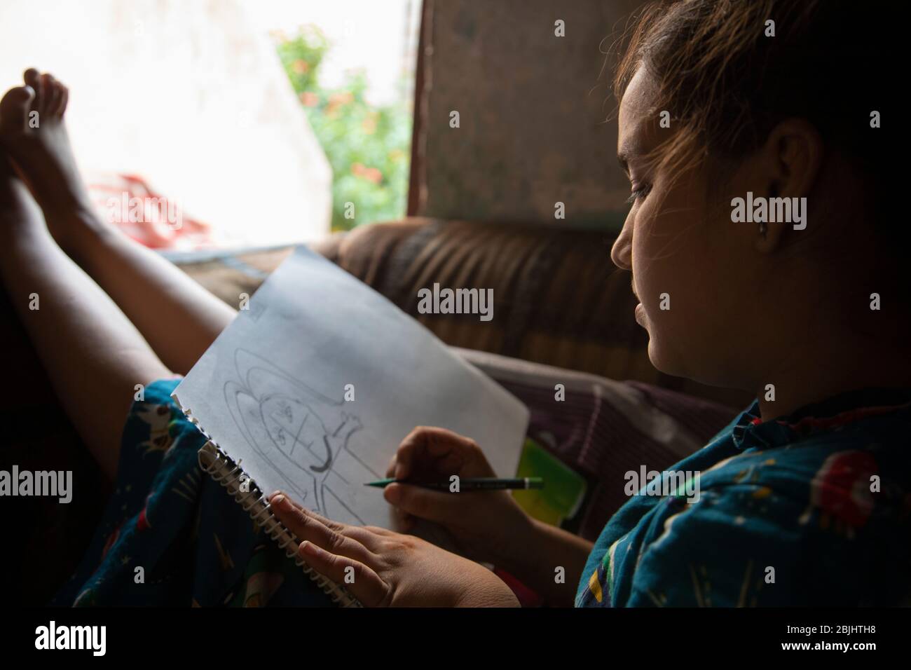 girl sitting on the sofa and drawing on a paper Stock Photo - Alamy