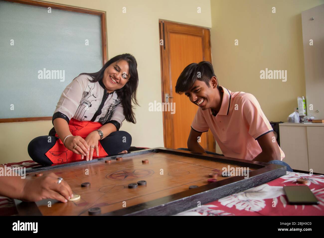 Son playing carrom-board with his parents at home Stock Photo - Alamy