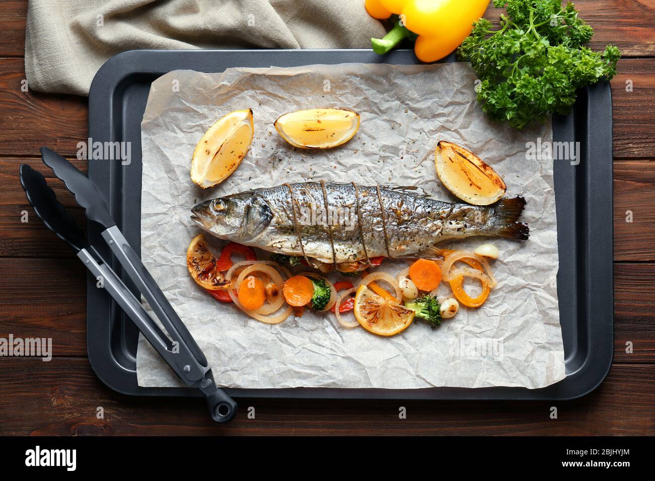 Baking sheet with sea bass fish on wooden table Stock Photo - Alamy