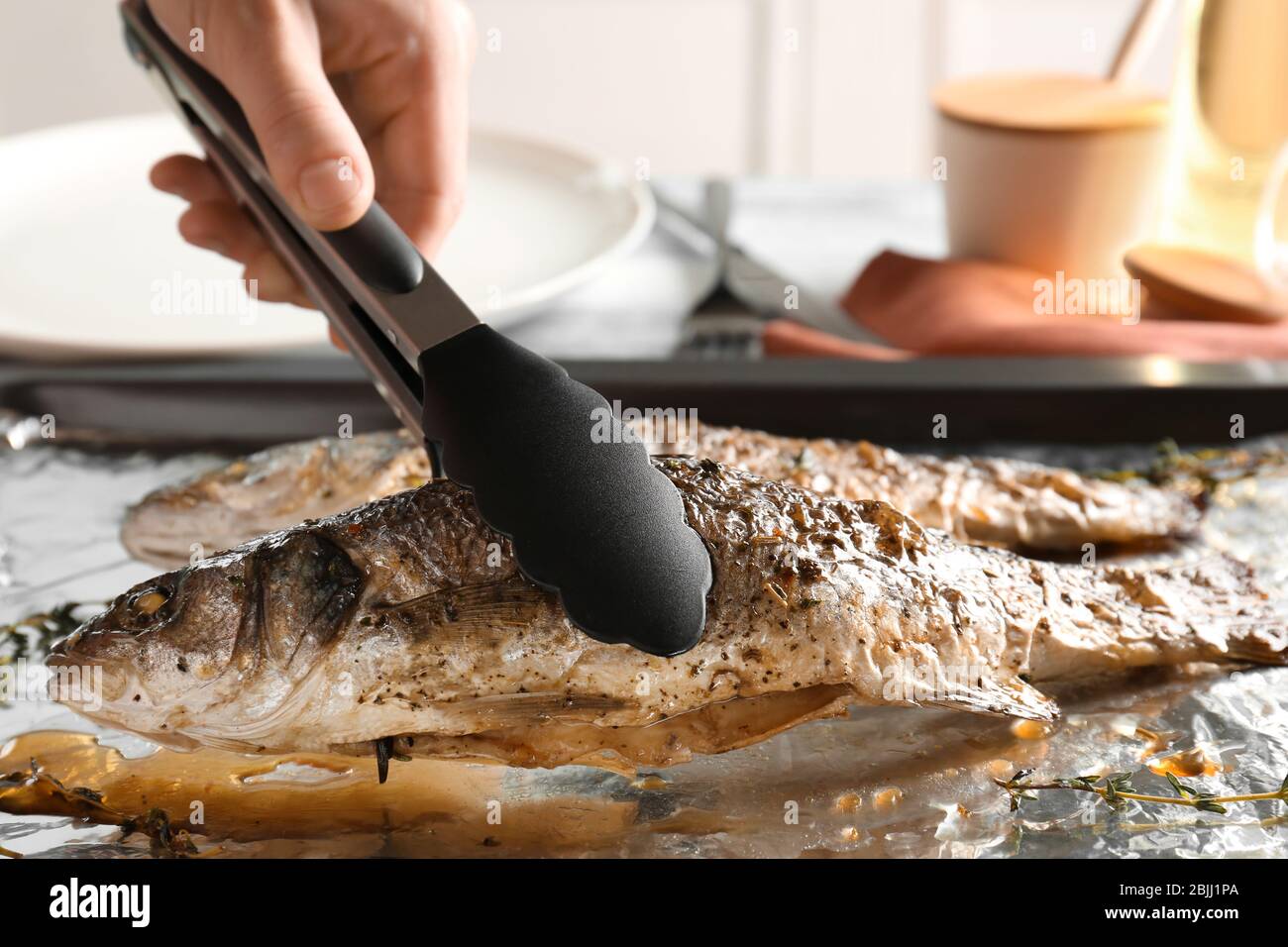 Woman taking tasty fish from baking tray using tongs, closeup Stock ...