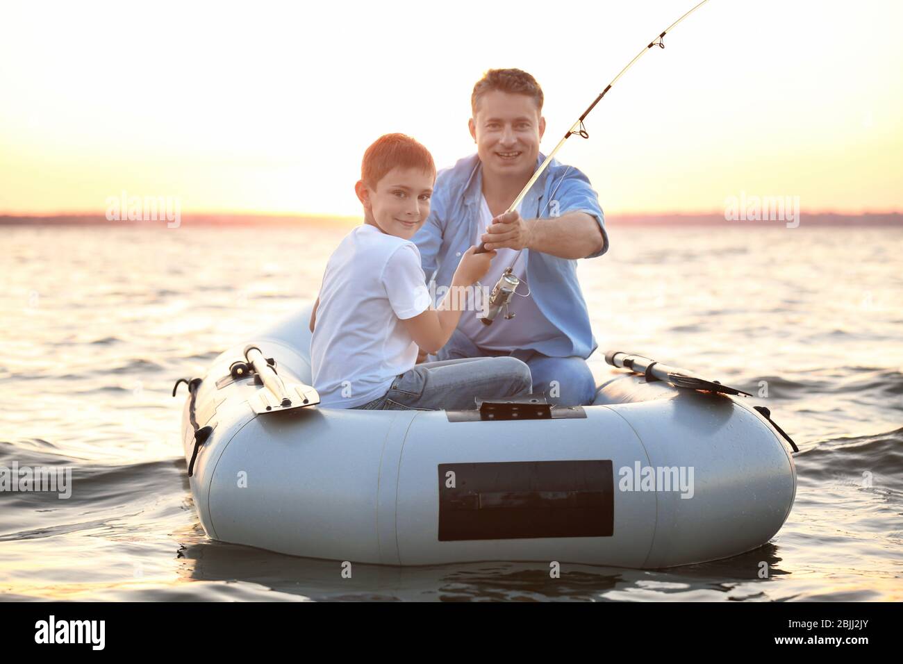 Dad and son fishing from inflatable boat on river Stock Photo - Alamy