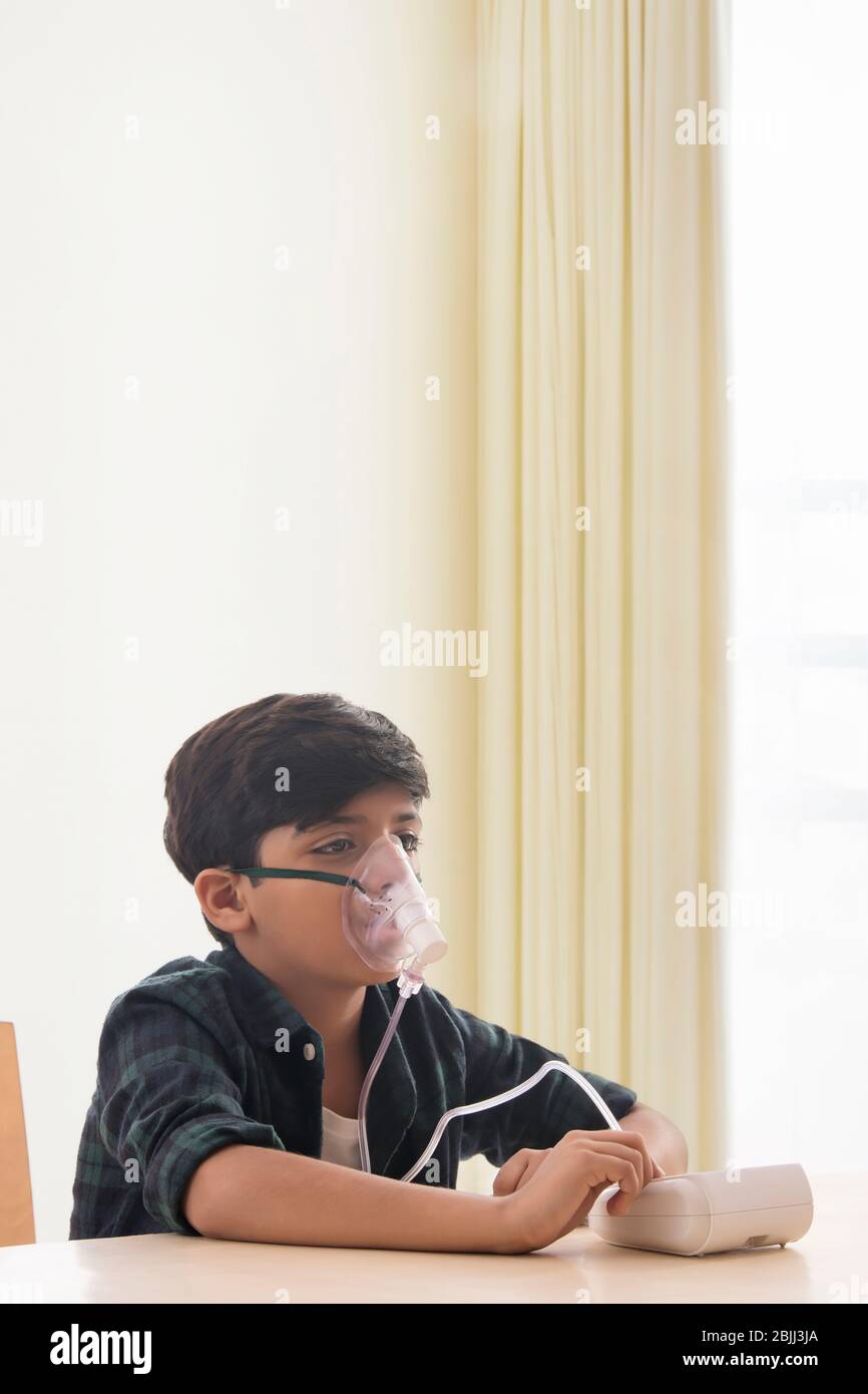 Young boy sitting and inhaling through a nebuliser at home. (Children ...
