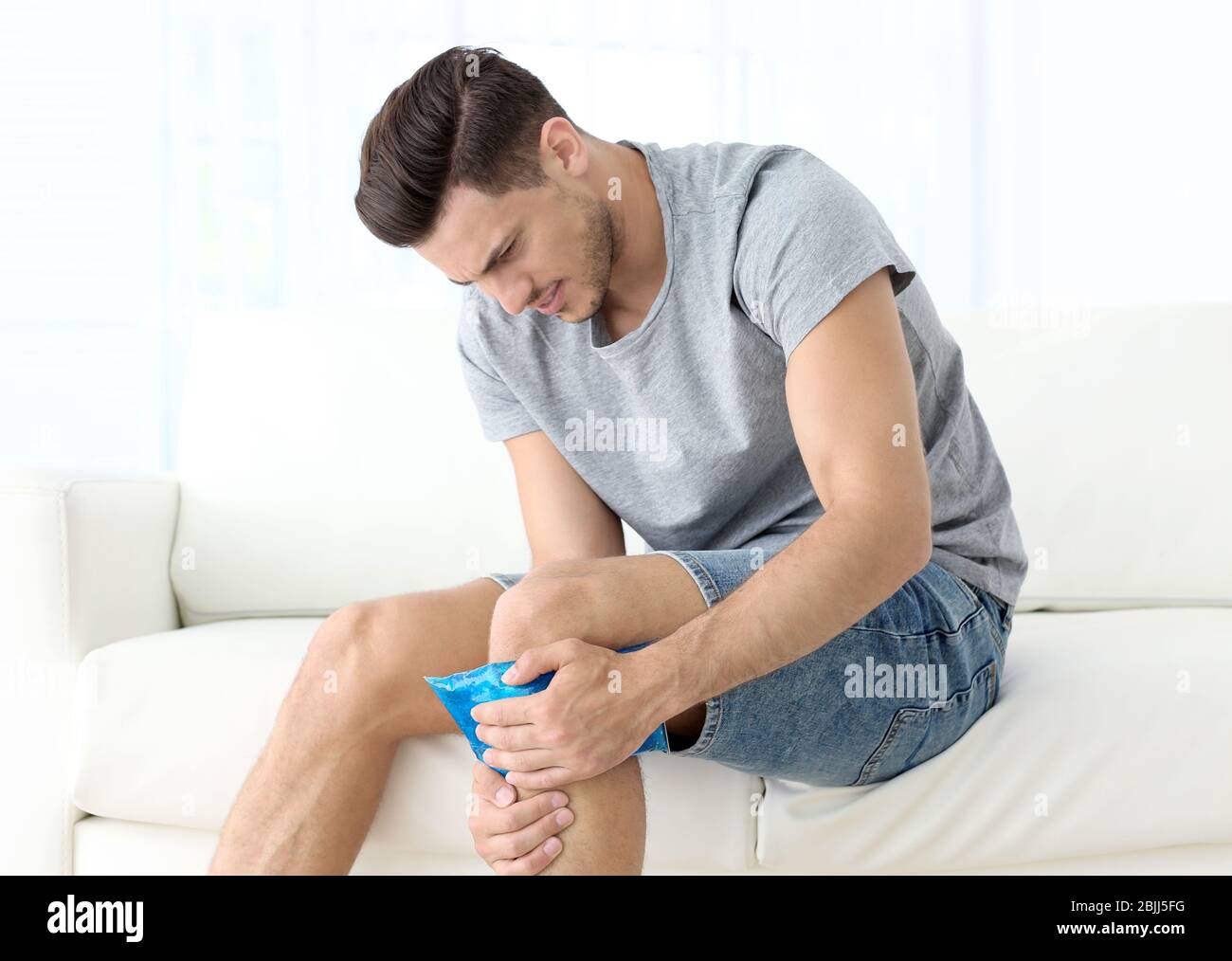 Young man applying cold compress to leg at home Stock Photo - Alamy