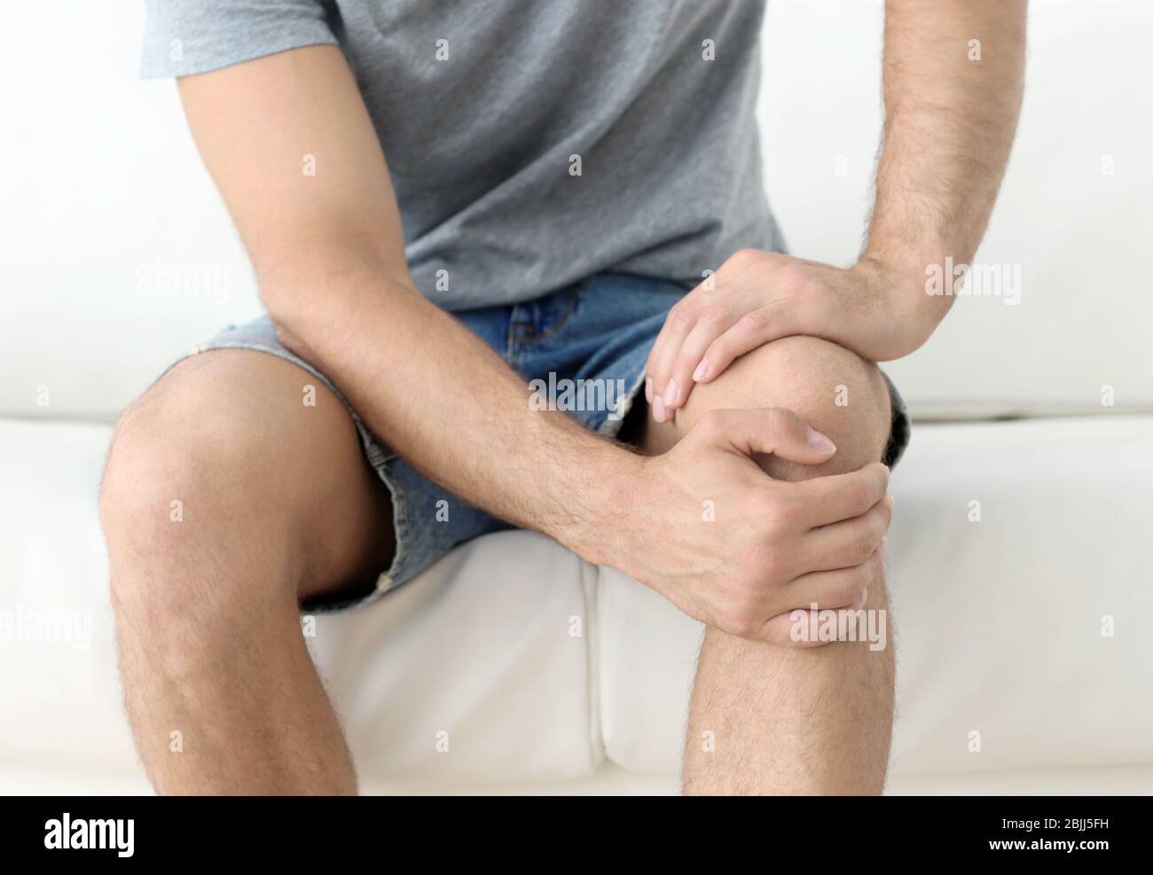 Young man suffering from leg pain at home Stock Photo - Alamy