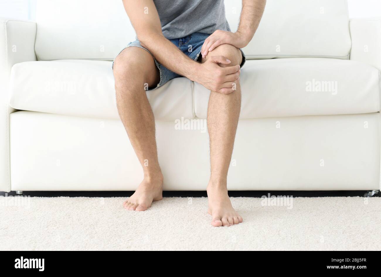 Young man suffering from leg pain at home Stock Photo - Alamy