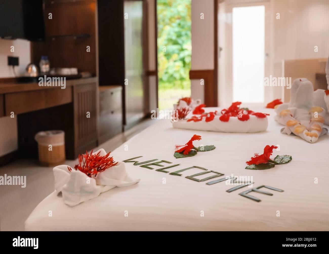 Word WELCOME and beautiful flowers on bed in hotel room Stock Photo - Alamy