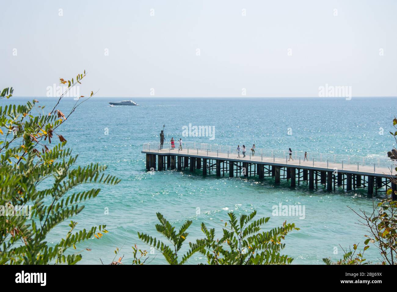 People walking on a pier with statue of Poseidon, bridge near the beach ...