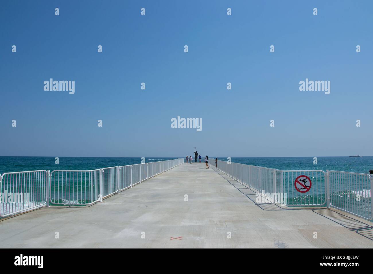 People walking on a pier with statue of Poseidon, bridge near the beach ...