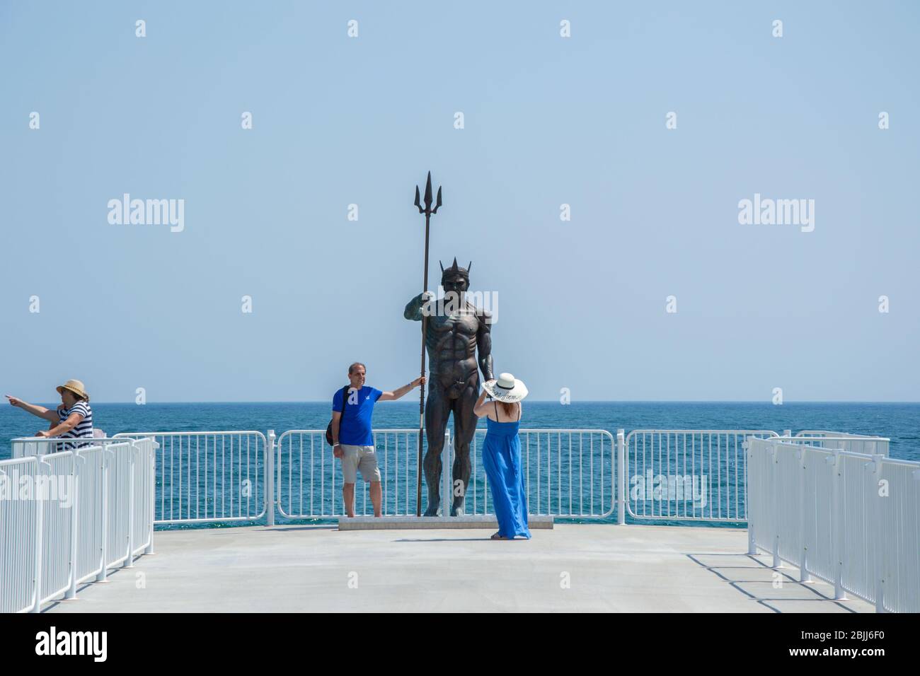 People walking on a pier with statue of Poseidon, bridge near the beach ...