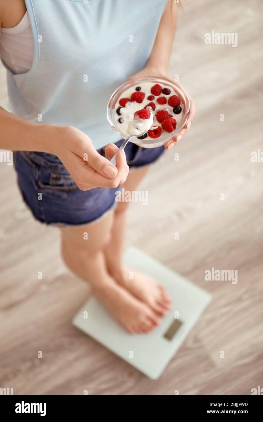 Young woman on floor scales eating yogurt at home Stock Photo - Alamy