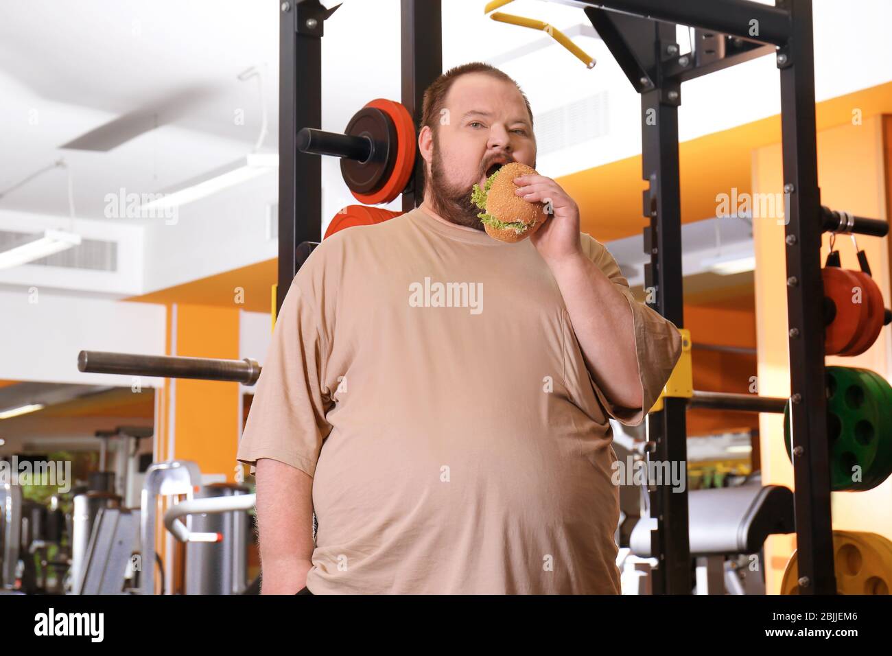 Overweight man eating sandwich in gym Stock Photo - Alamy