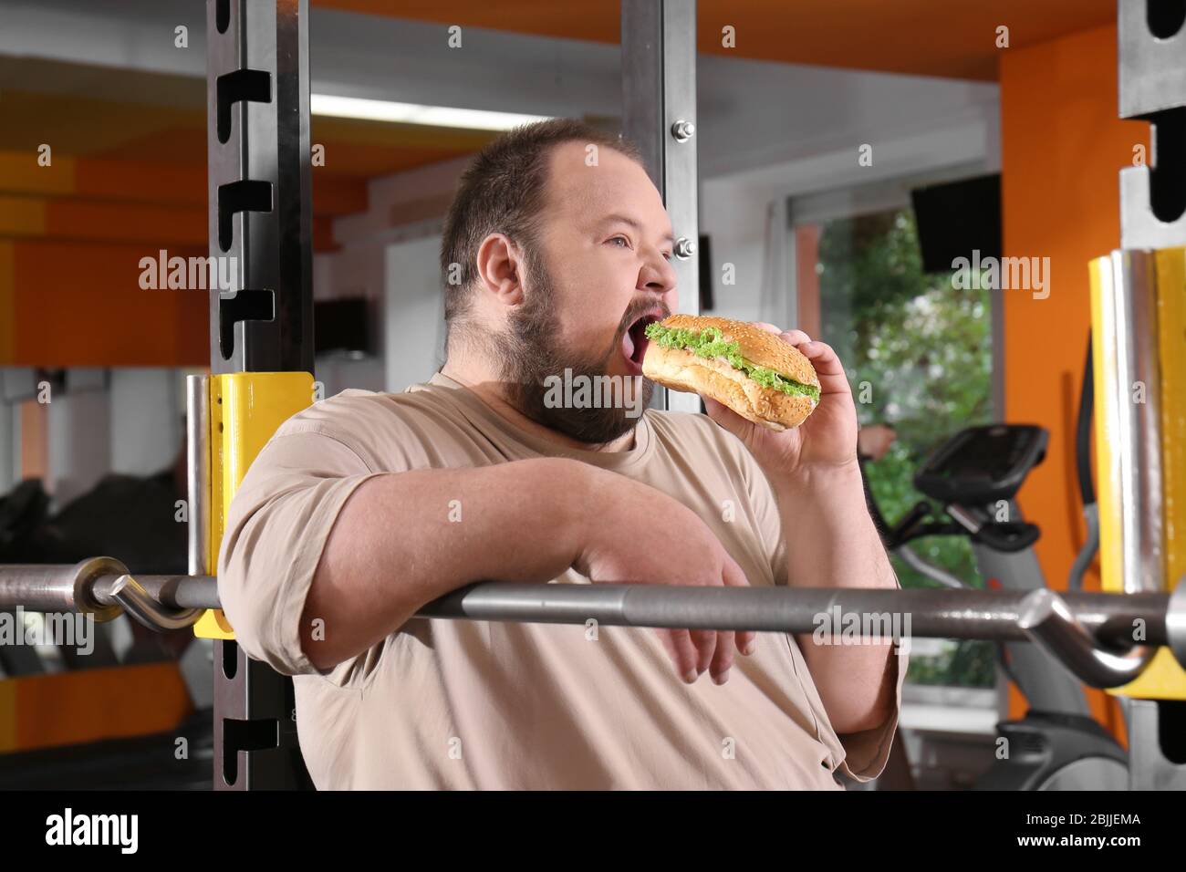 Overweight man eating sandwich in gym Stock Photo - Alamy