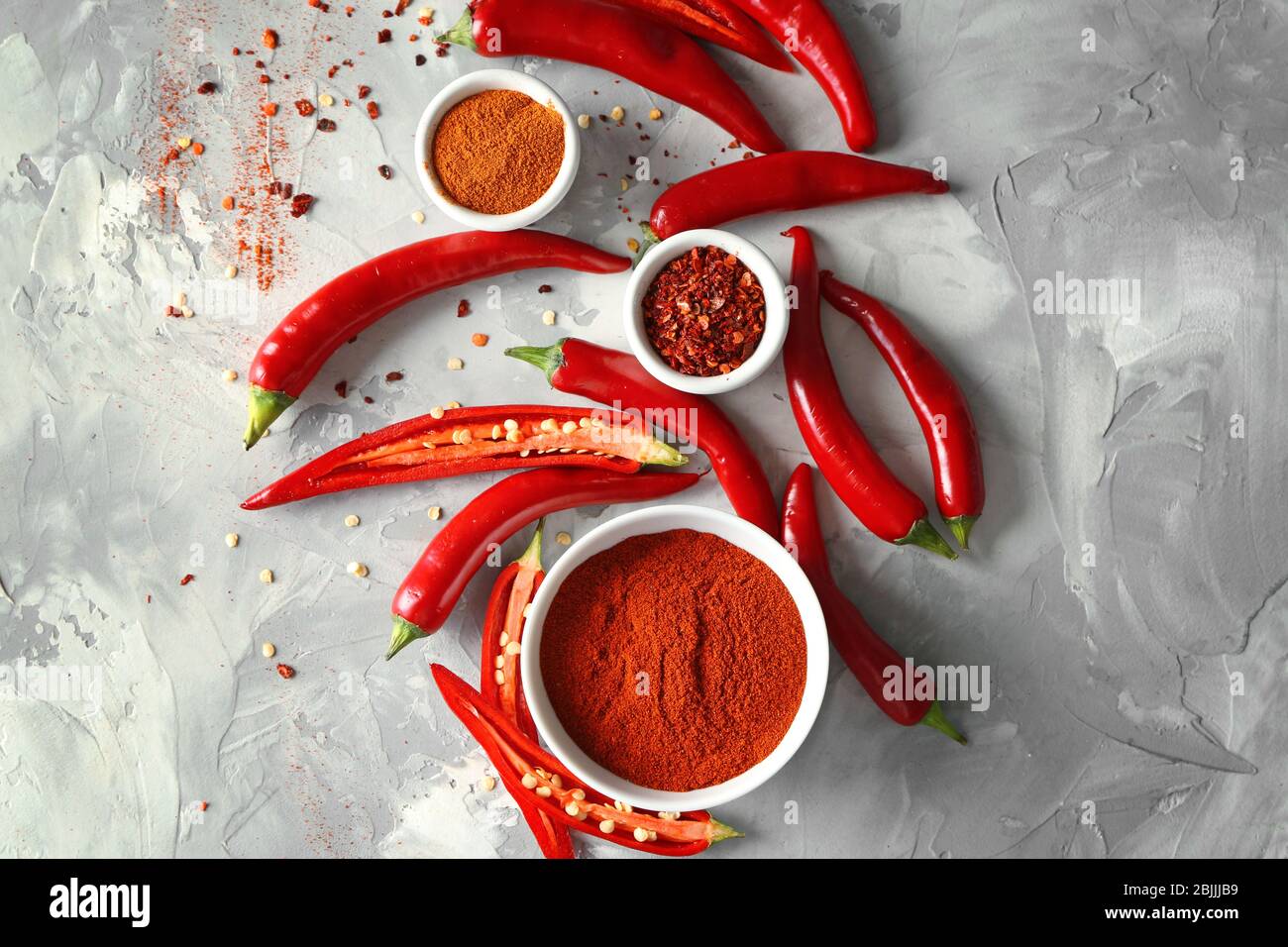 Composition with red chili powder, flakes and pepper pods on grey ...