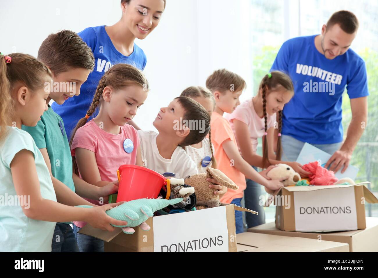 Happy volunteers with children sorting donation goods indoors Stock ...