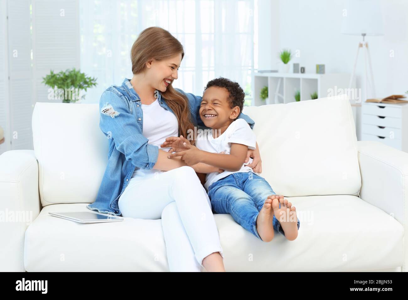 Happy mother with adopted African-American boy sitting on couch at home ...