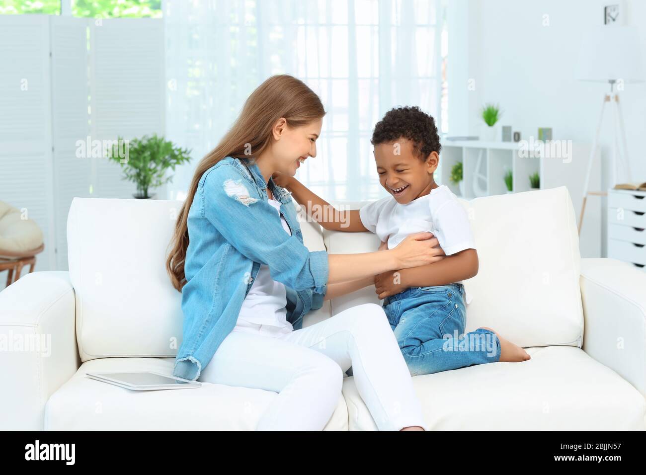 Happy mother with adopted African-American boy sitting on couch at home ...