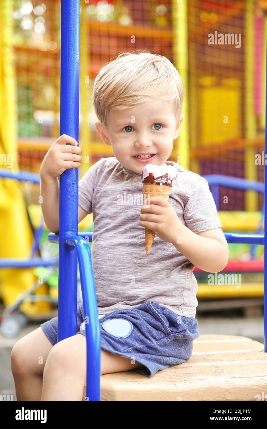 Cute little boy eating ice-cream while playing on swings in park Stock ...