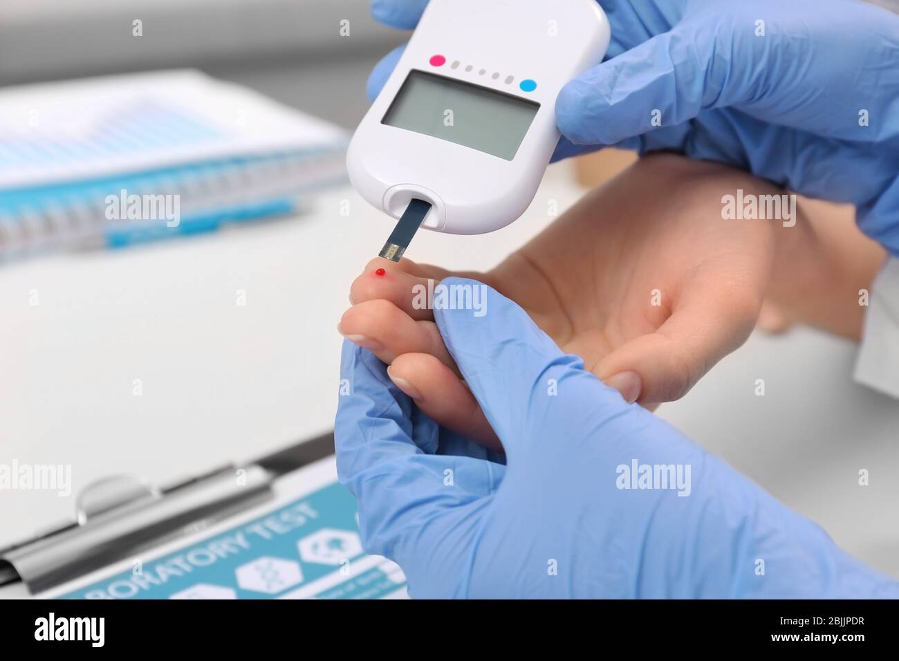Medical technician in latex gloves testing patient's glucose level with ...
