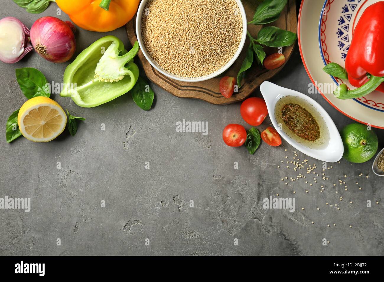 Composition with raw quinoa, oil and fresh vegetables on grey ...