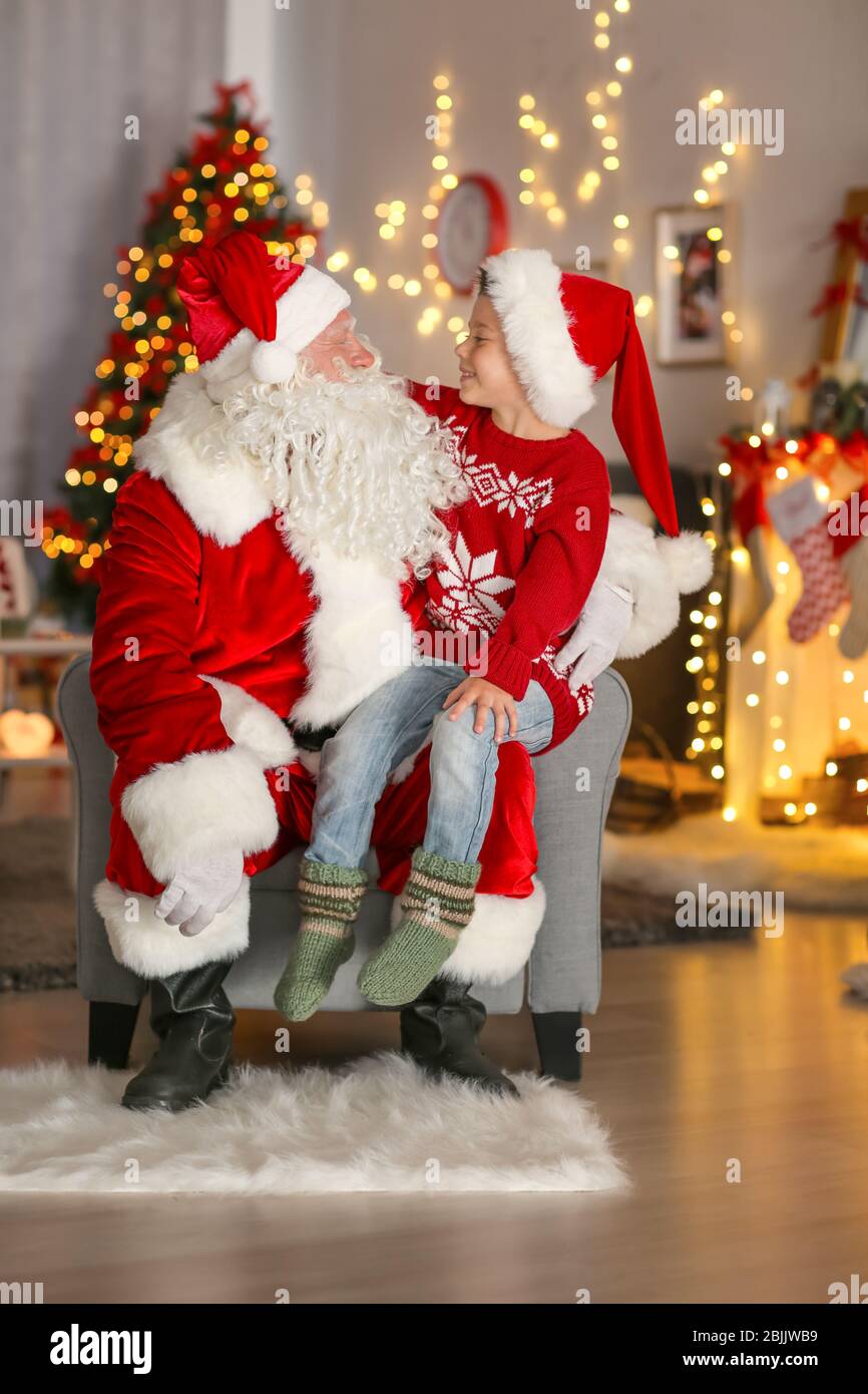Happy little boy sitting on Santa's lap in room with beautiful ...