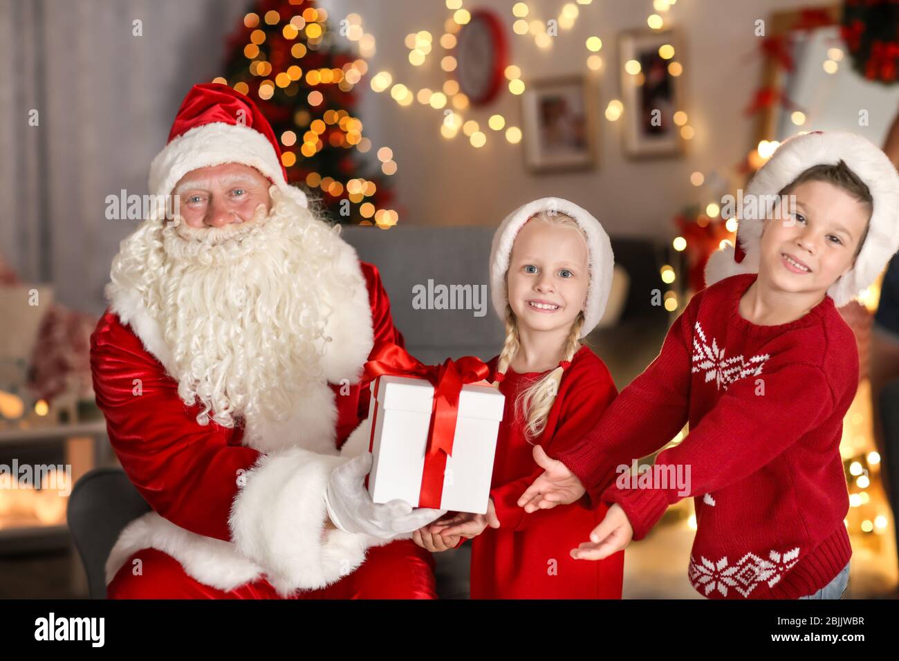 Santa Claus giving present to children in room with beautiful Christmas ...