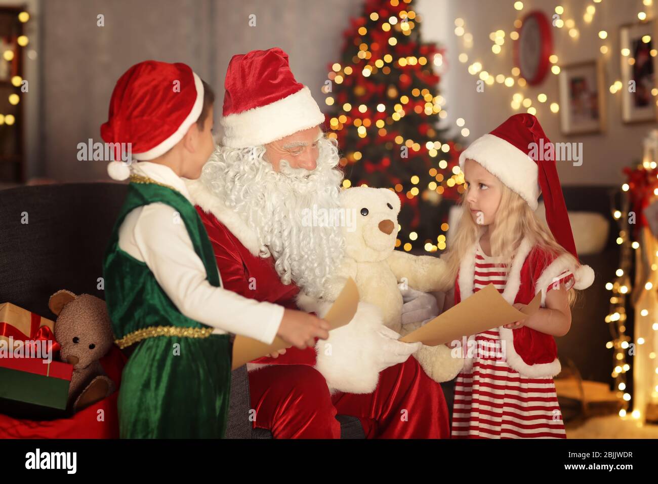 Cute elf kids showing letters to Santa in room with beautiful Christmas ...