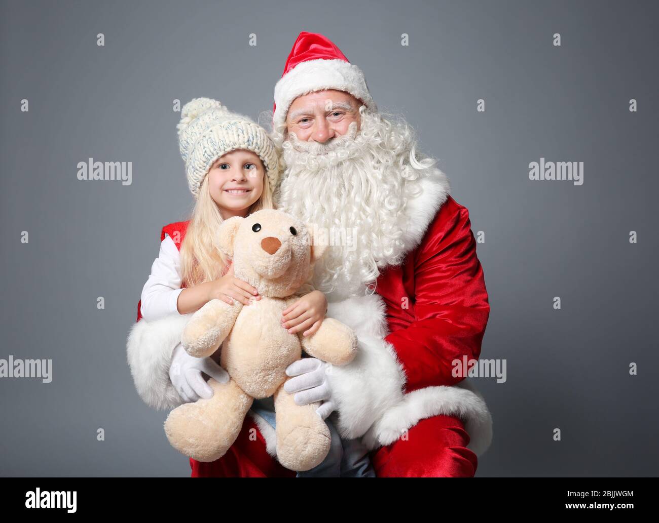 Cute little girl with teddy bear sitting on Santa's lap against color ...