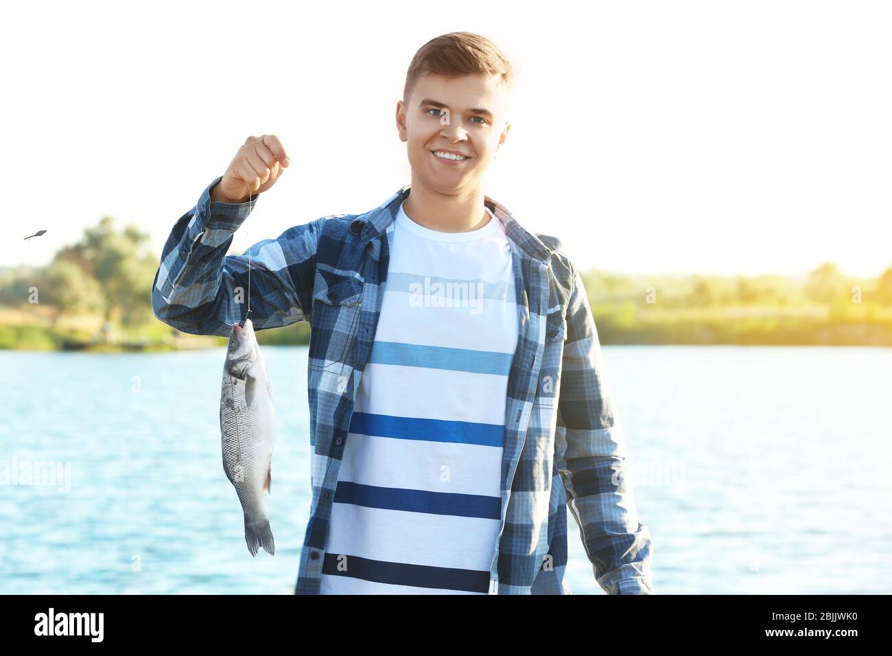 Young man holding freshly caught fish near river Stock Photo - Alamy