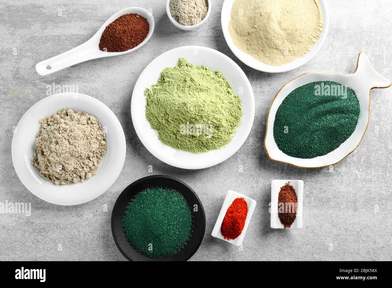 Various colorful superfood powders in kitchenware on grey background ...