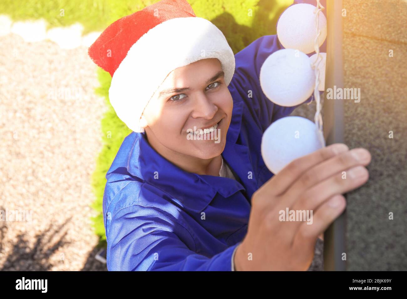 Man in Santa hat decorating facade of house with garland for Christmas ...