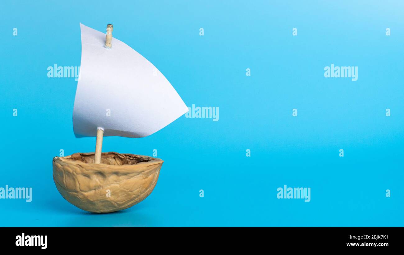 a boat made of nutshell with a white sail on the blue background ...