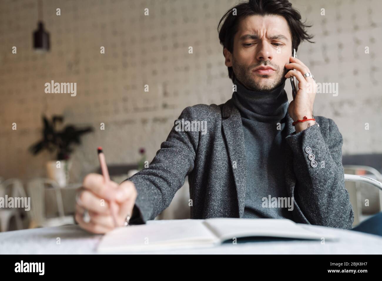 Image of handsome caucasian young man taking notes and talking on ...