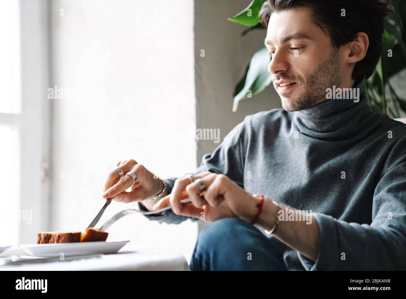 Image of handsome caucasian young man eating dessert while sitting at ...