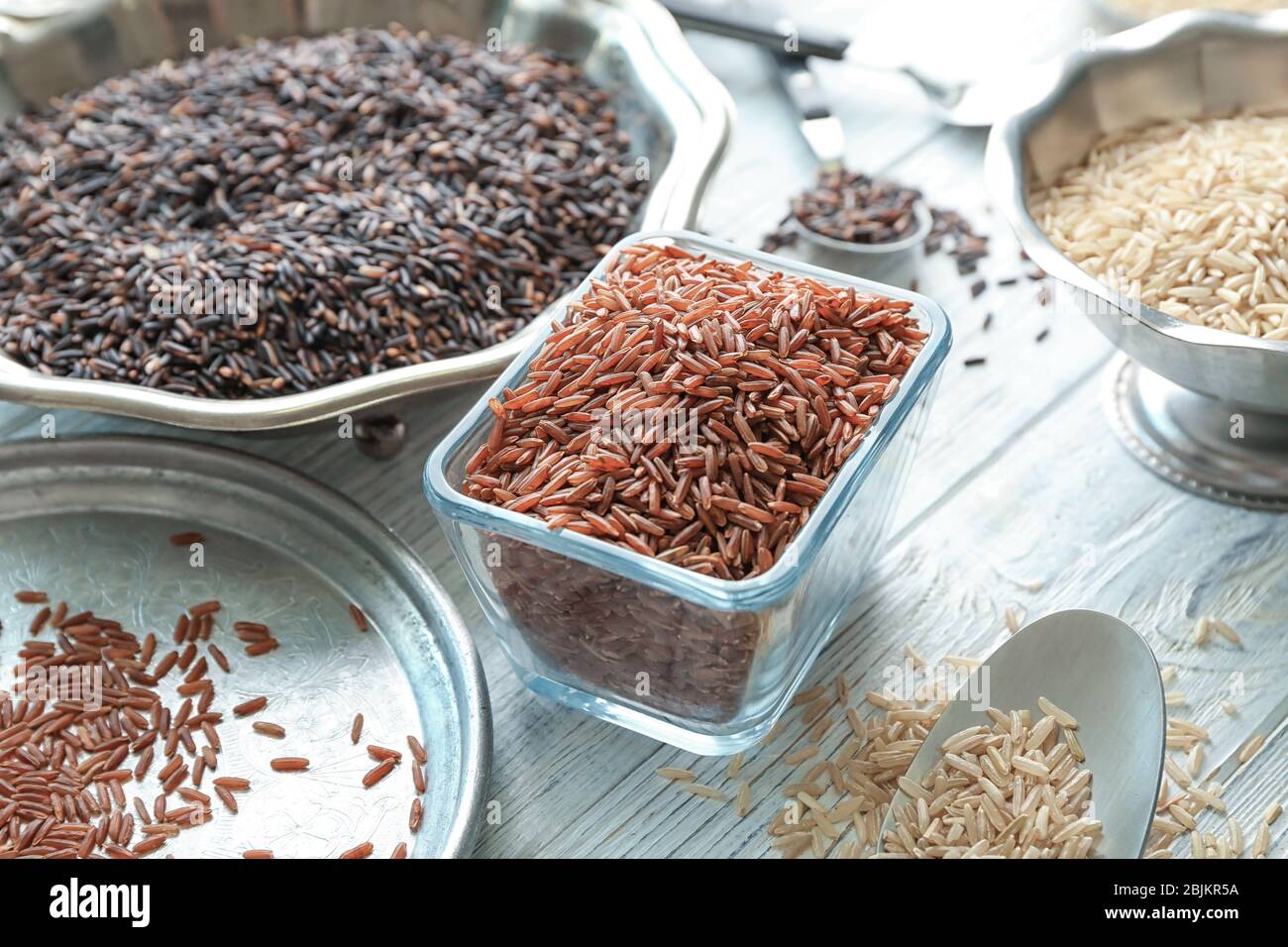 Different types of rice in bowls, plate and spoons on wooden table ...