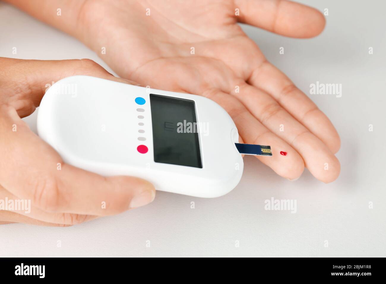 Woman testing glucose level with digital glucometer on white background ...