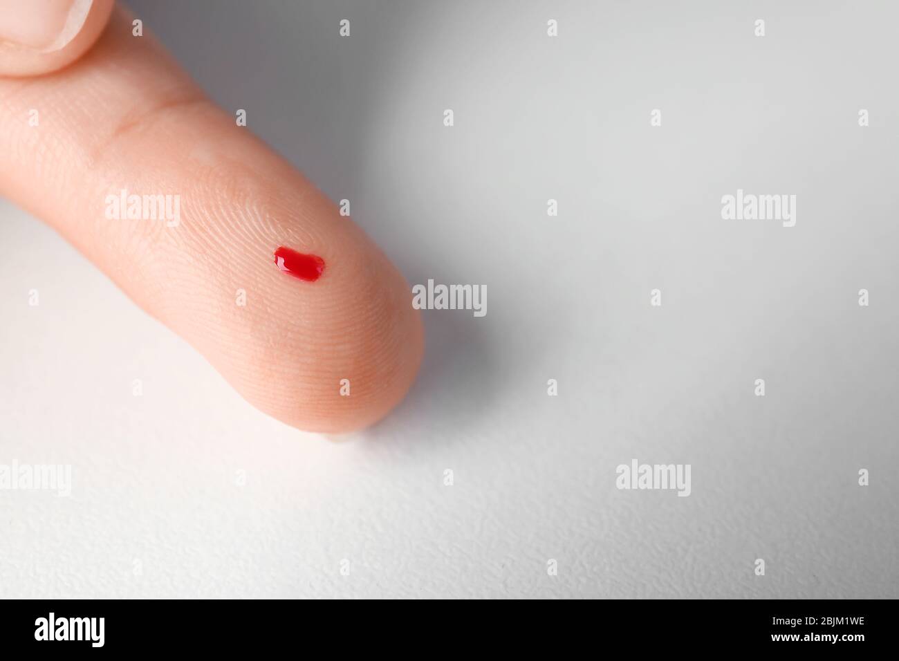 Finger of woman with blood drop for testing glucose level, on white ...
