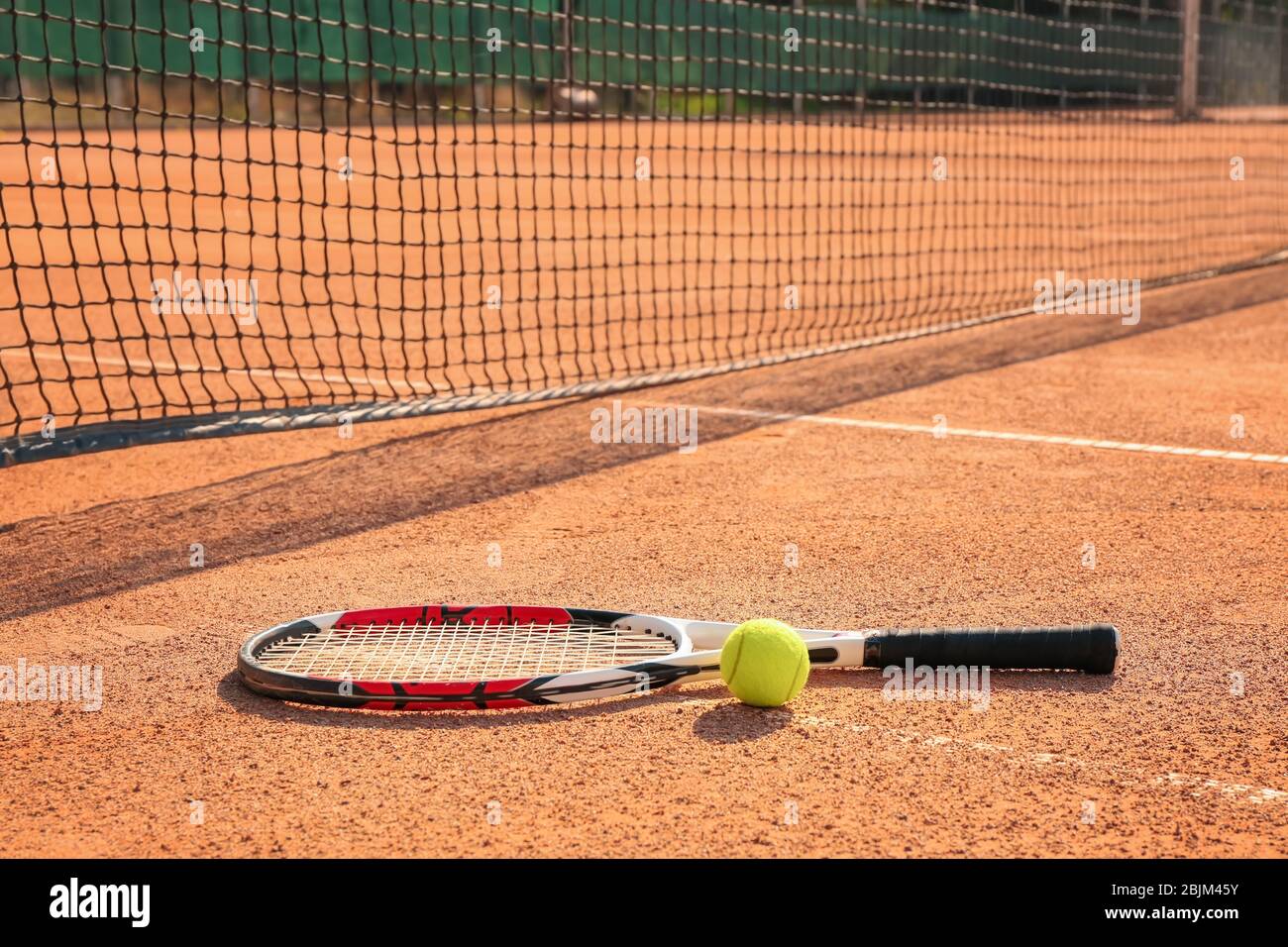 Tennis racket and ball near net on court Stock Photo - Alamy