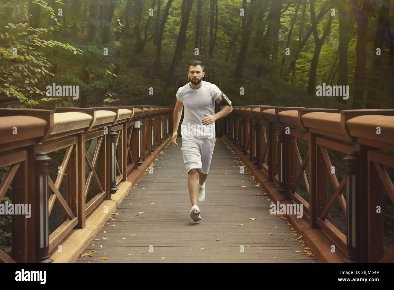 Sporty man running over bridge in park Stock Photo - Alamy