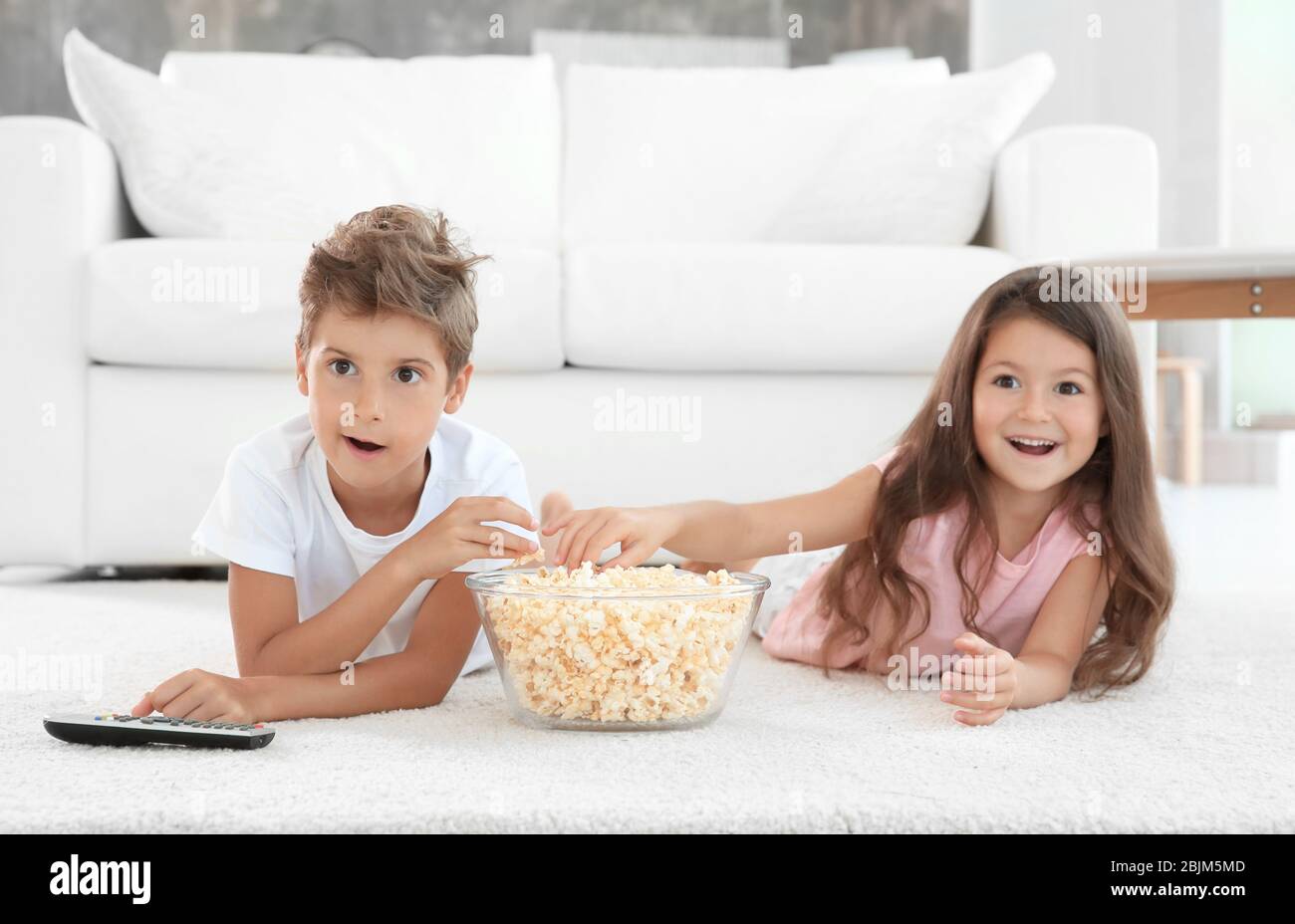 Cute children eating popcorn while watching TV on floor at home Stock ...
