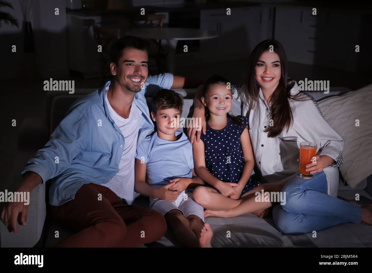 Happy family watching TV on sofa at night Stock Photo - Alamy