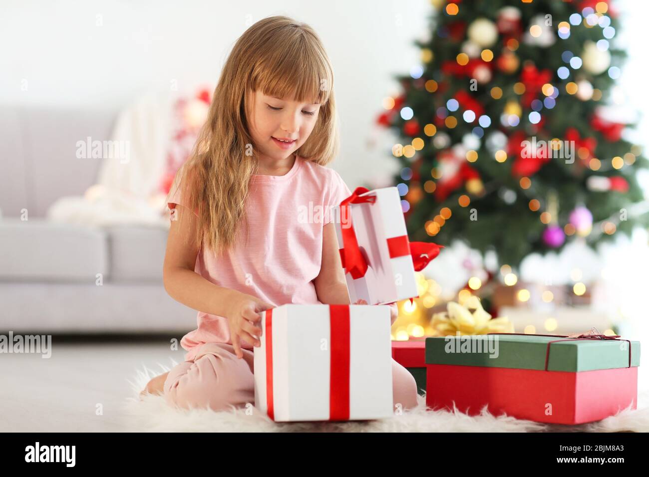 Cute little girl opening gift box in room decorated for Christmas Stock ...