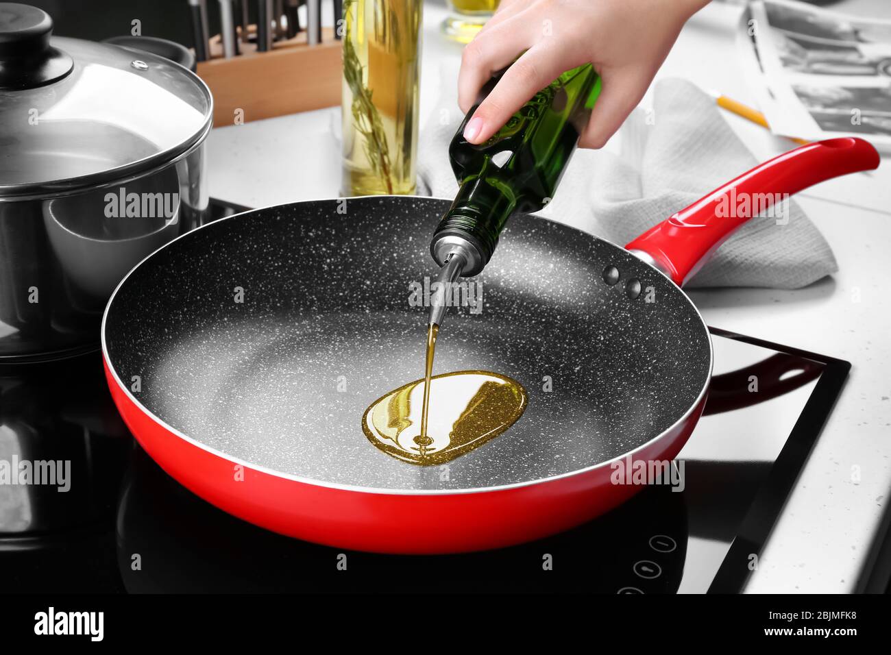 Woman pouring oil from bottle into frying pan in kitchen Stock Photo ...