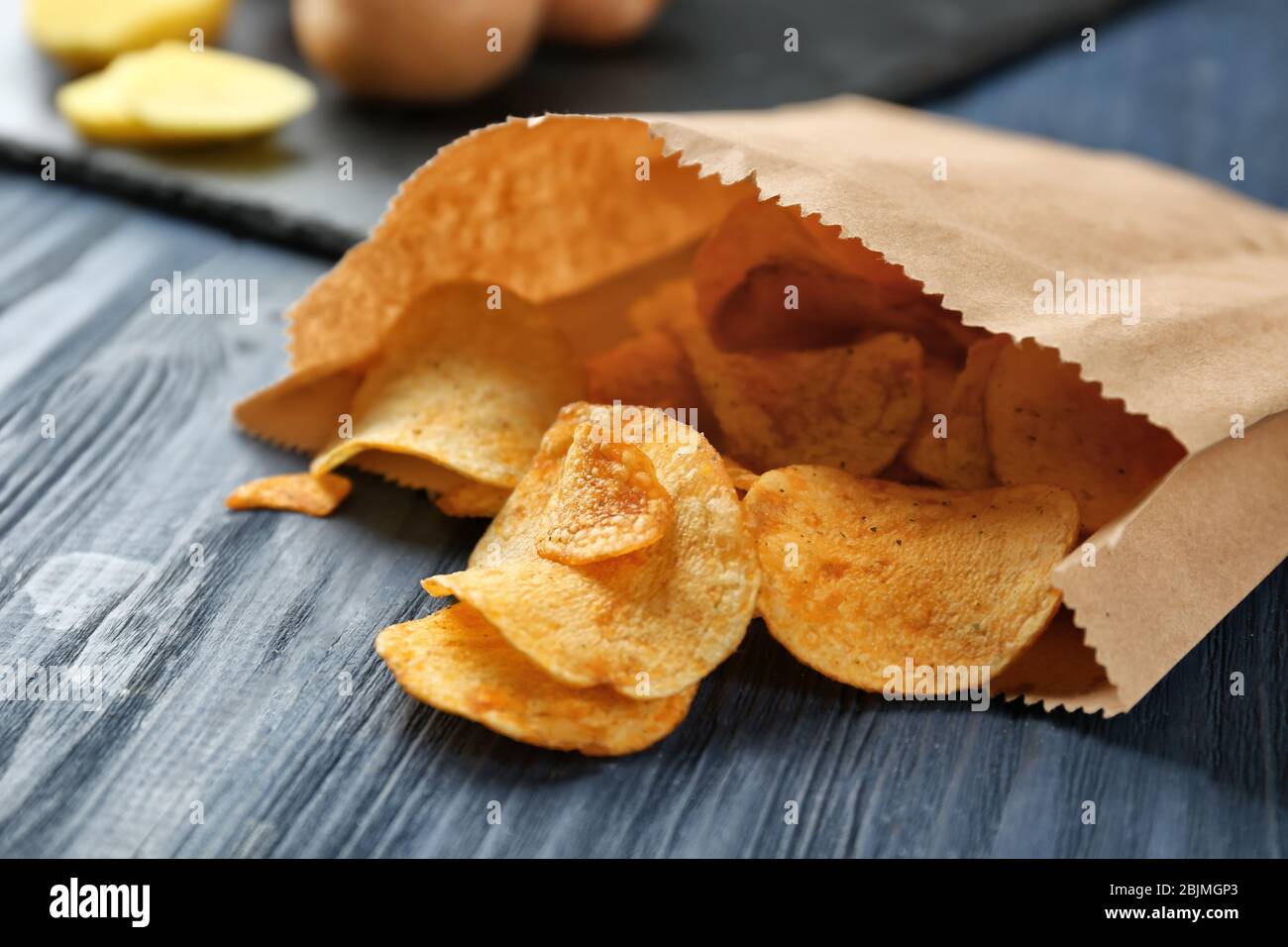 Paper bag with yummy crispy potato chips on wooden table Stock Photo ...