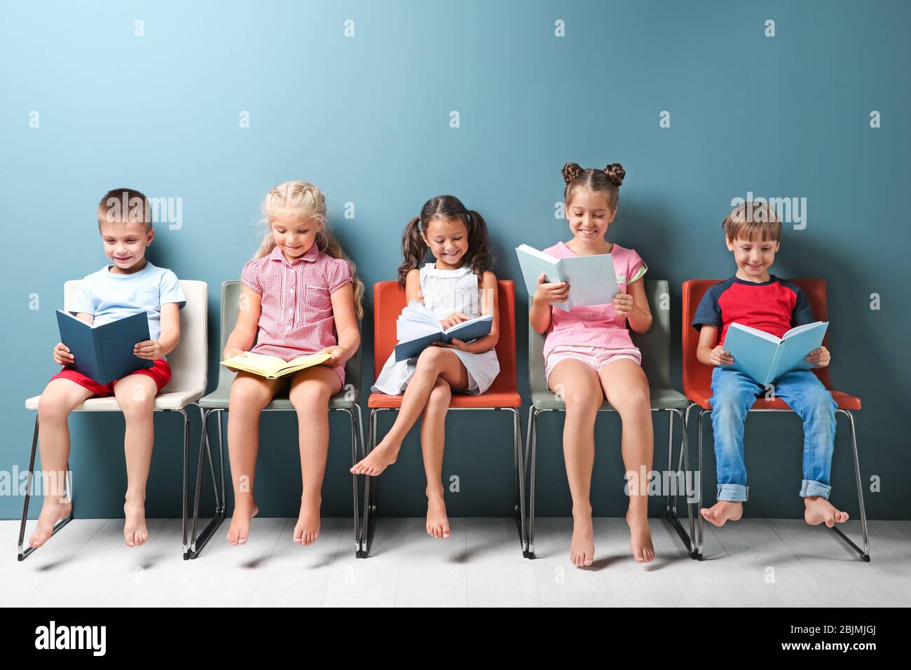 Cute little children reading books while sitting near color wall Stock ...