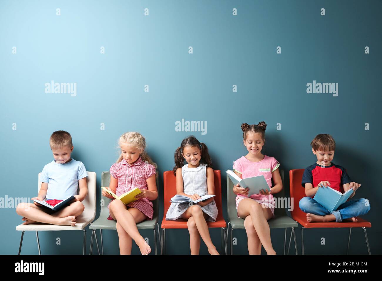 Cute little children reading books while sitting near color wall Stock ...