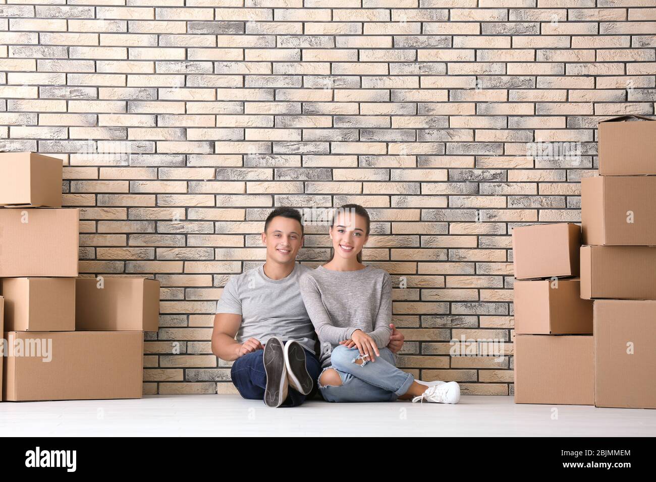 Happy young couple and moving boxes near brick wall Stock Photo - Alamy